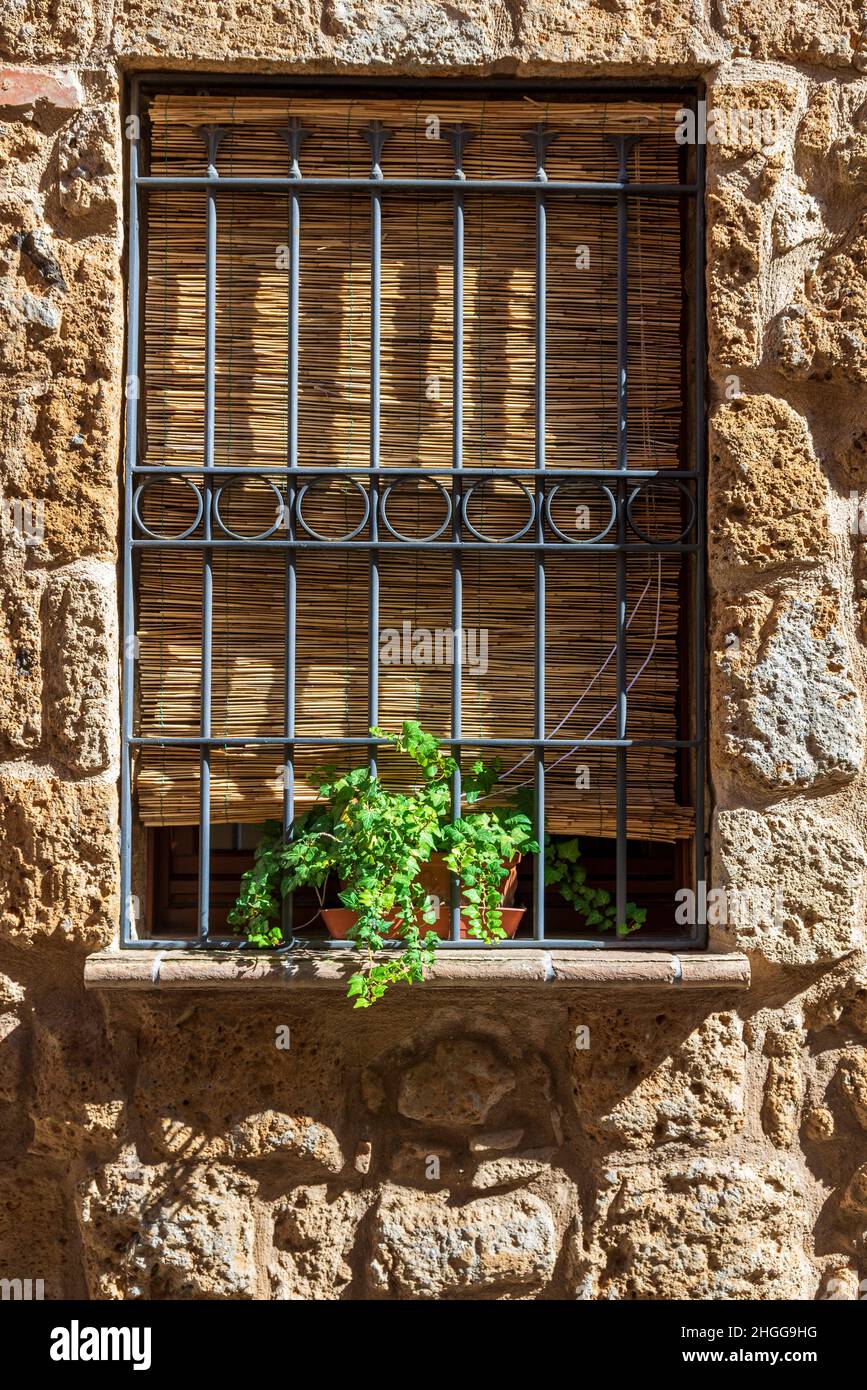 Pretty Italian window, set in a stone wall with metal grill and plant ...