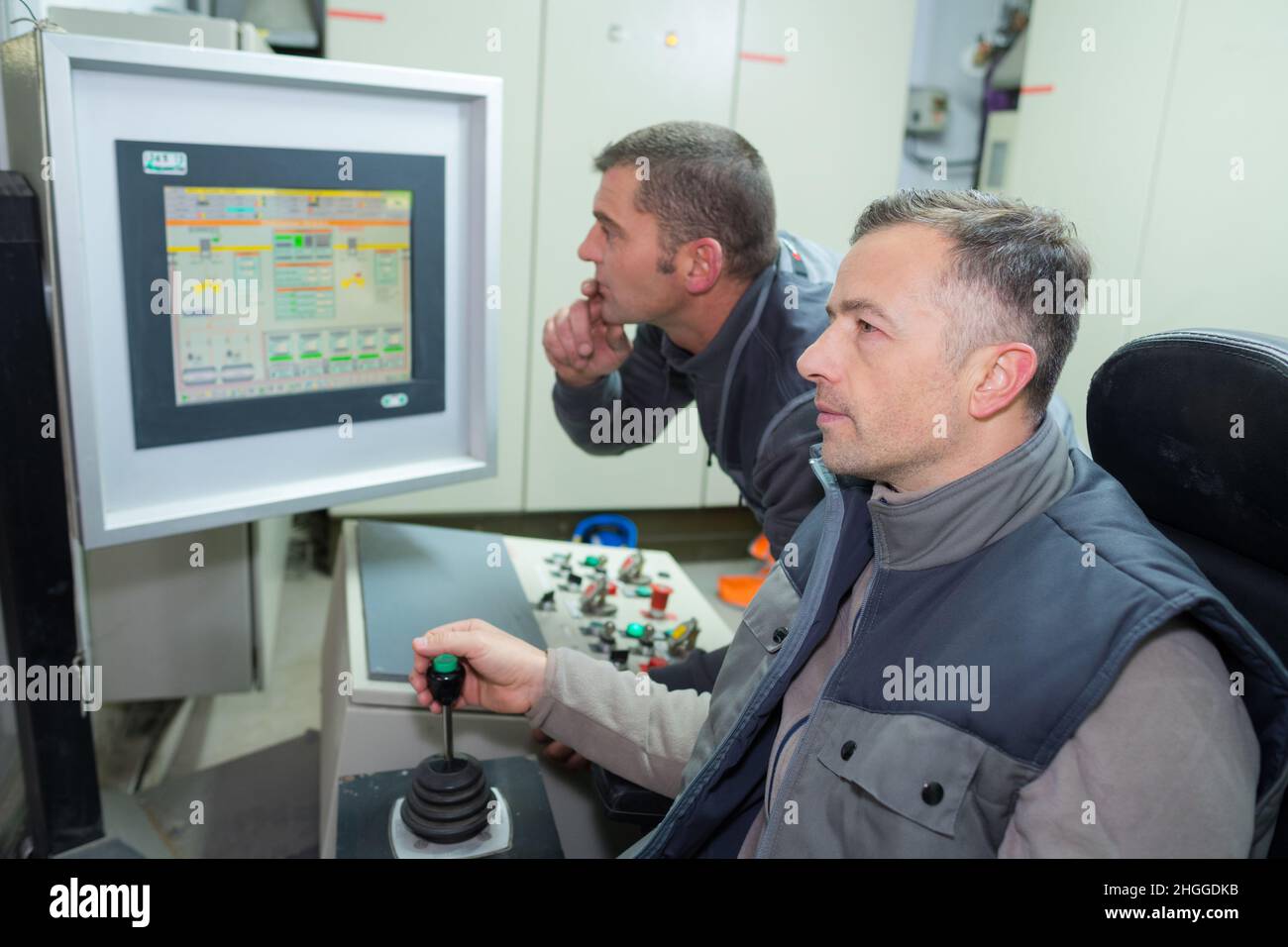 worker consulting monitor while colleague operates controls Stock Photo ...