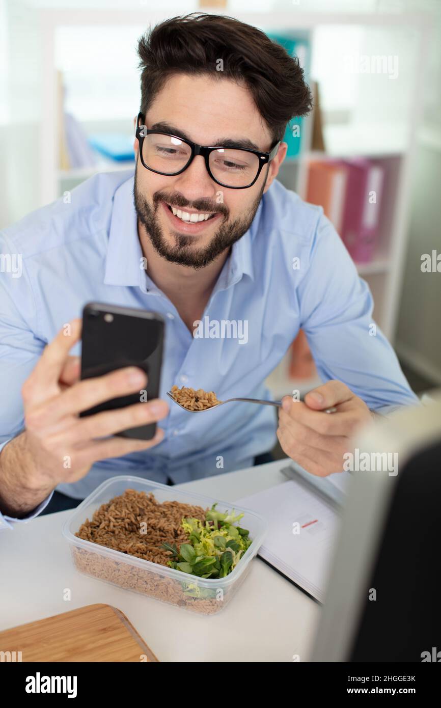 man eating lunch at his desk and using smartphone Stock Photo - Alamy