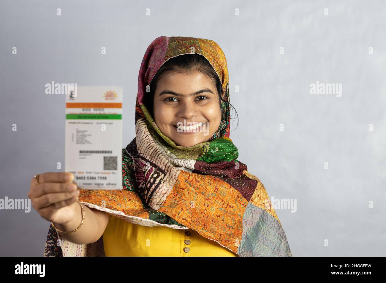 An Indian young woman smiling with Aadhaar card in hand on white ...