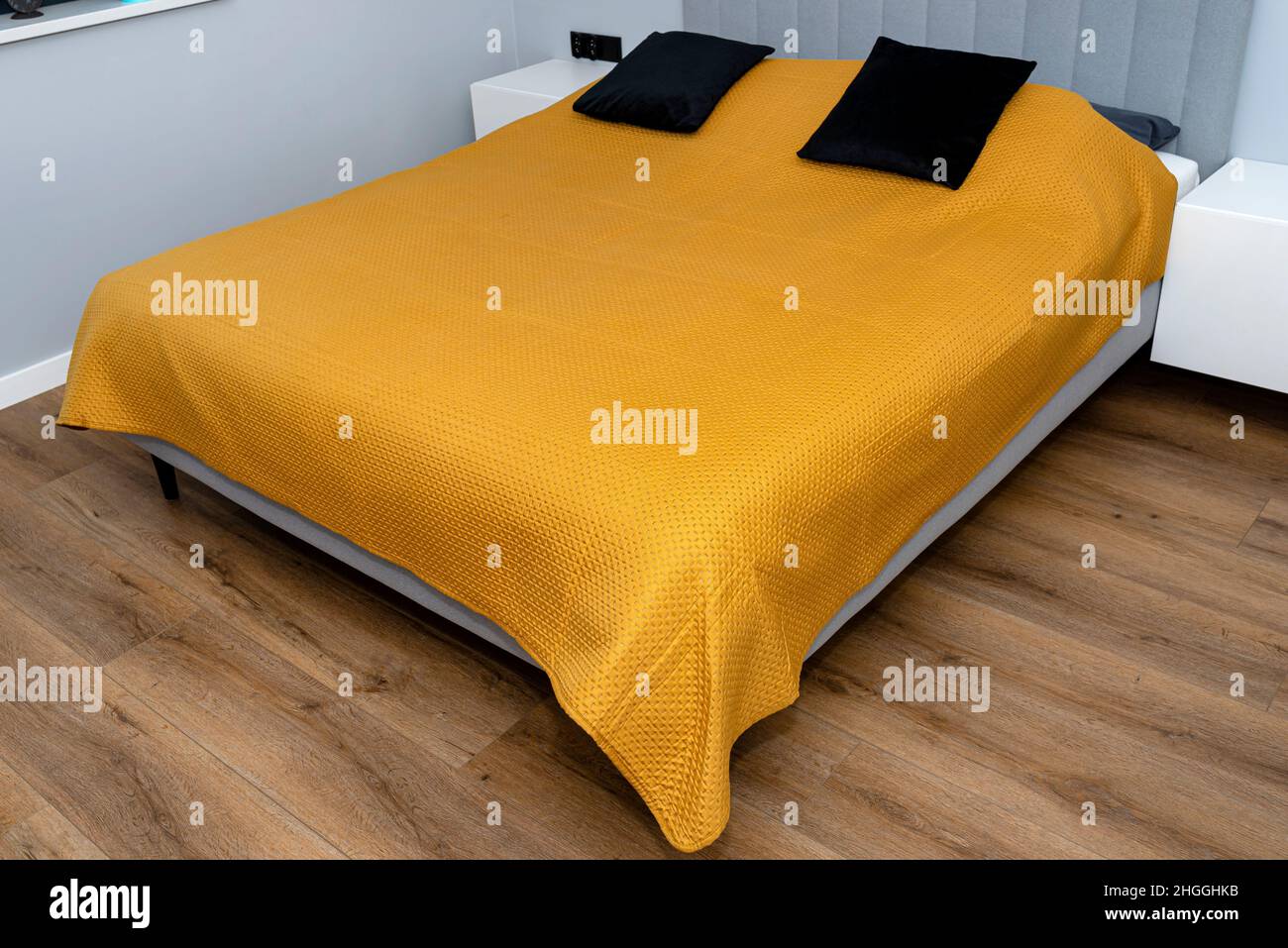 A bed in a modern bedroom with a mustard bedspread, simple look Stock ...
