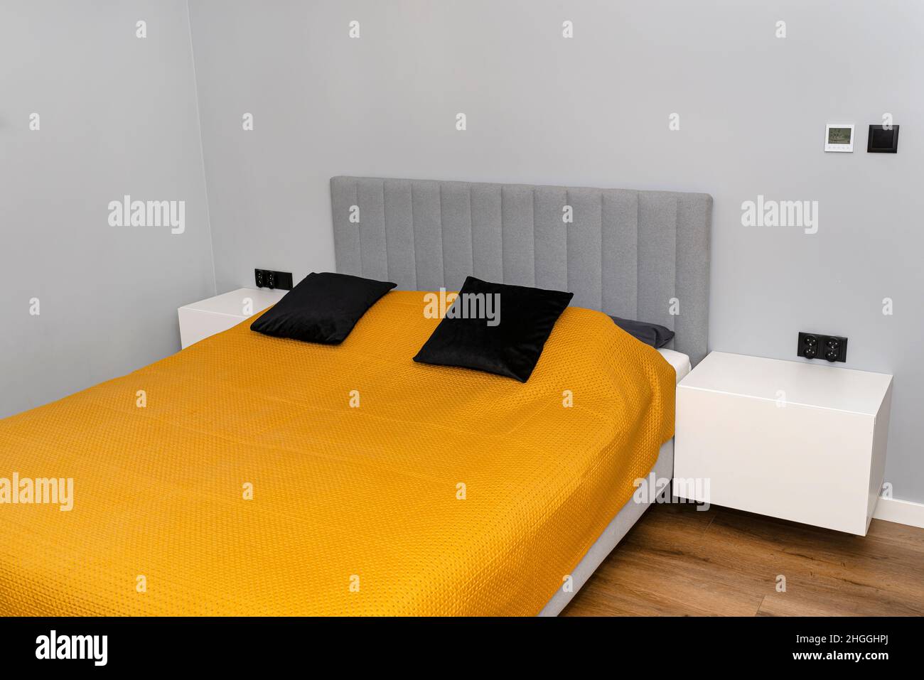 A bed in a modern bedroom with a mustard bedspread, simple look Stock ...