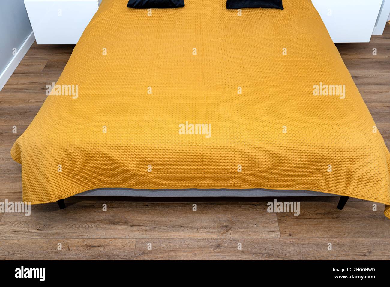A bed in a modern bedroom with a mustard bedspread, simple look Stock ...
