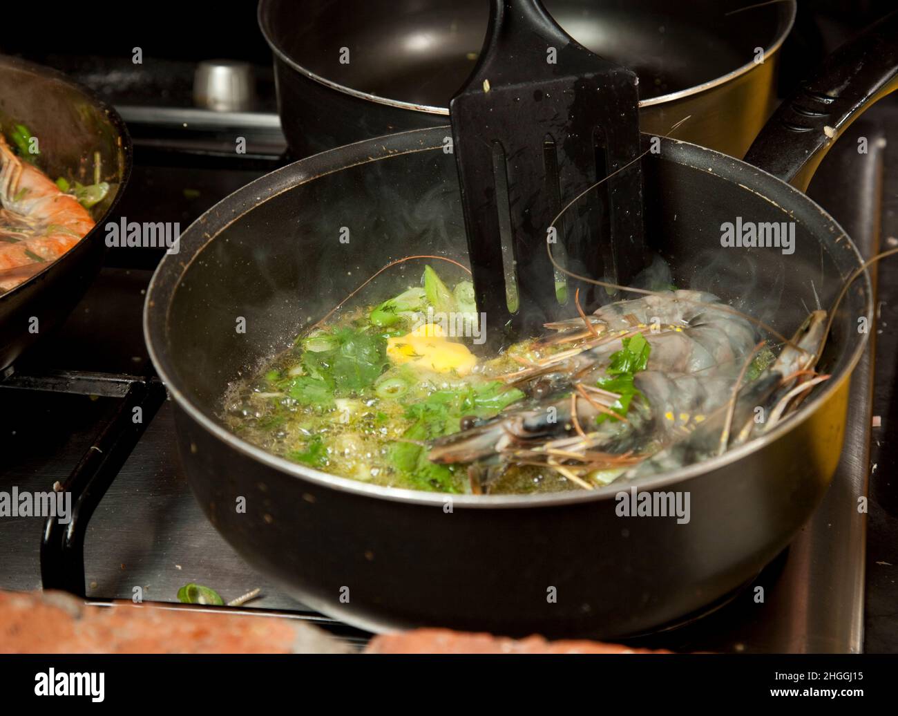 Fresh prawn being cooked in a pan with chopped spring onion on a stove ...
