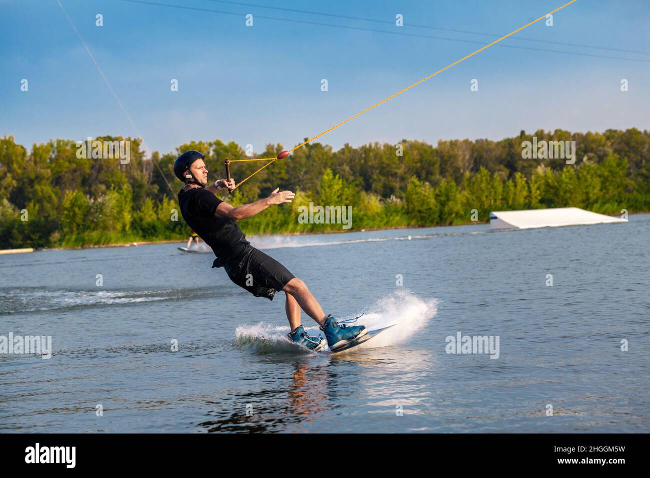 Focused man sliding on wakeboard on water surface holding tow rope with ...