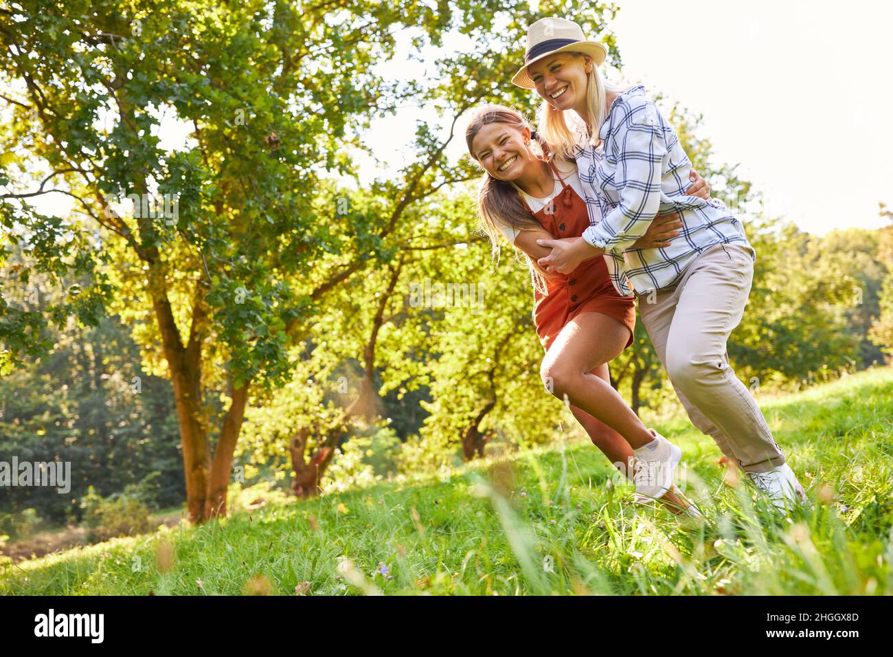 Mother and daughter have fun together and hop around on a meadow in ...