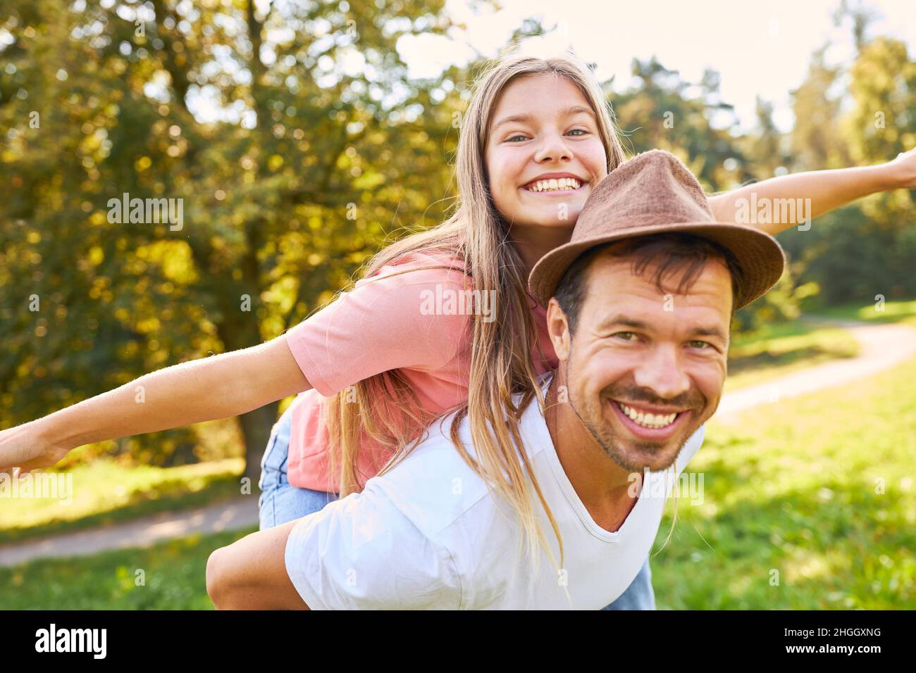 Happy daughter having fun piggybacking on father's back in summer in ...