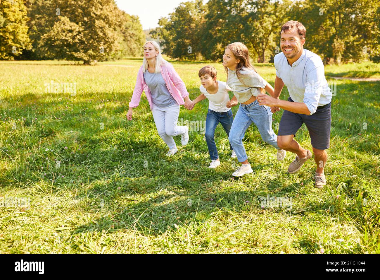 Happy family running together across a green meadow in summer in nature ...