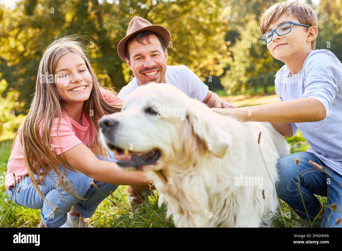 Father and two children pet their retriever dog in the park in summer ...