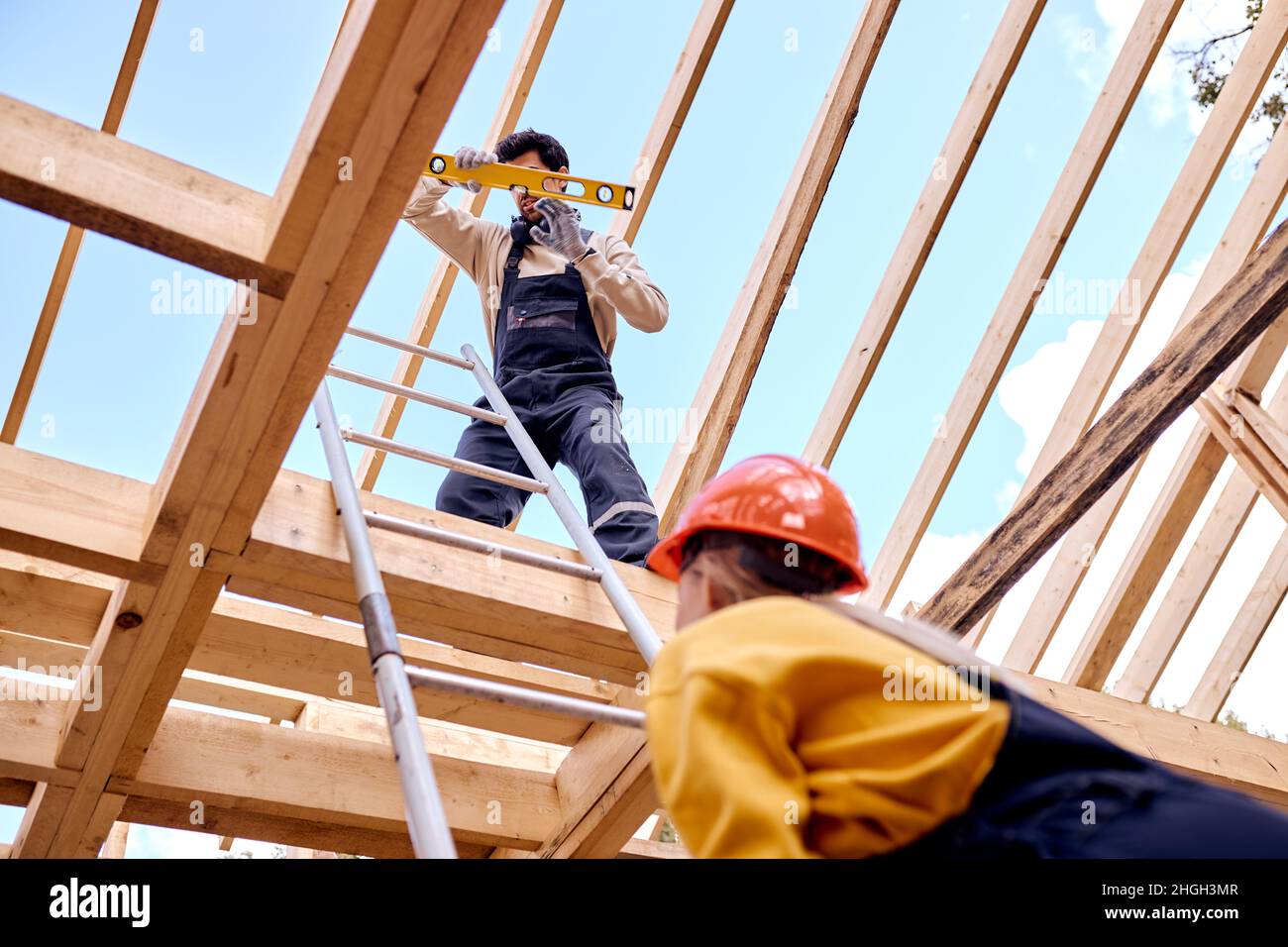 two contractors in working clothes uniform climb to the roof of wooden ...