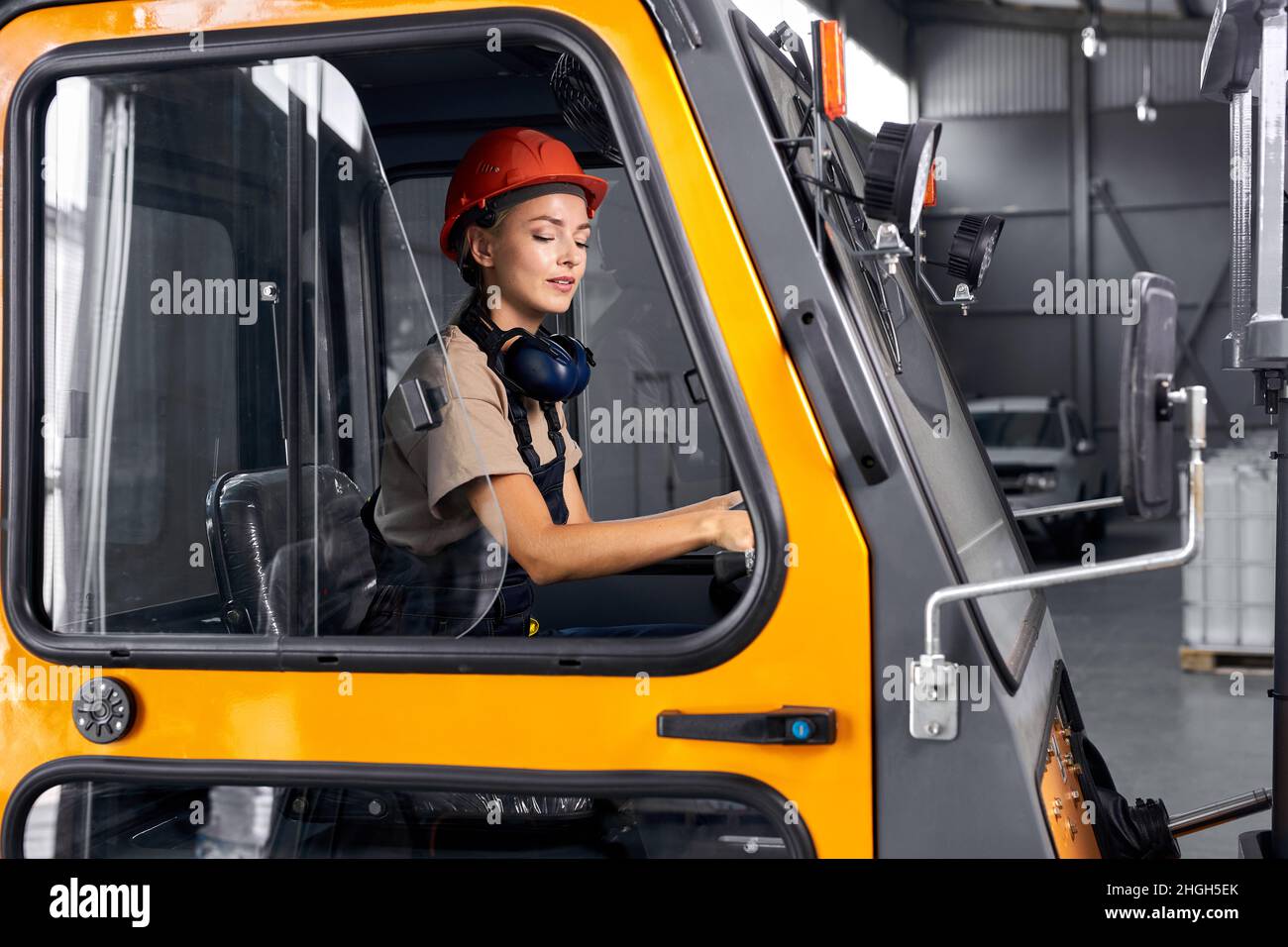 Female worker driving loader in industrial container warehouse, looking ...