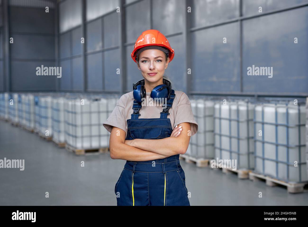industrial woman engineer in hardhat standing in factory with arms ...