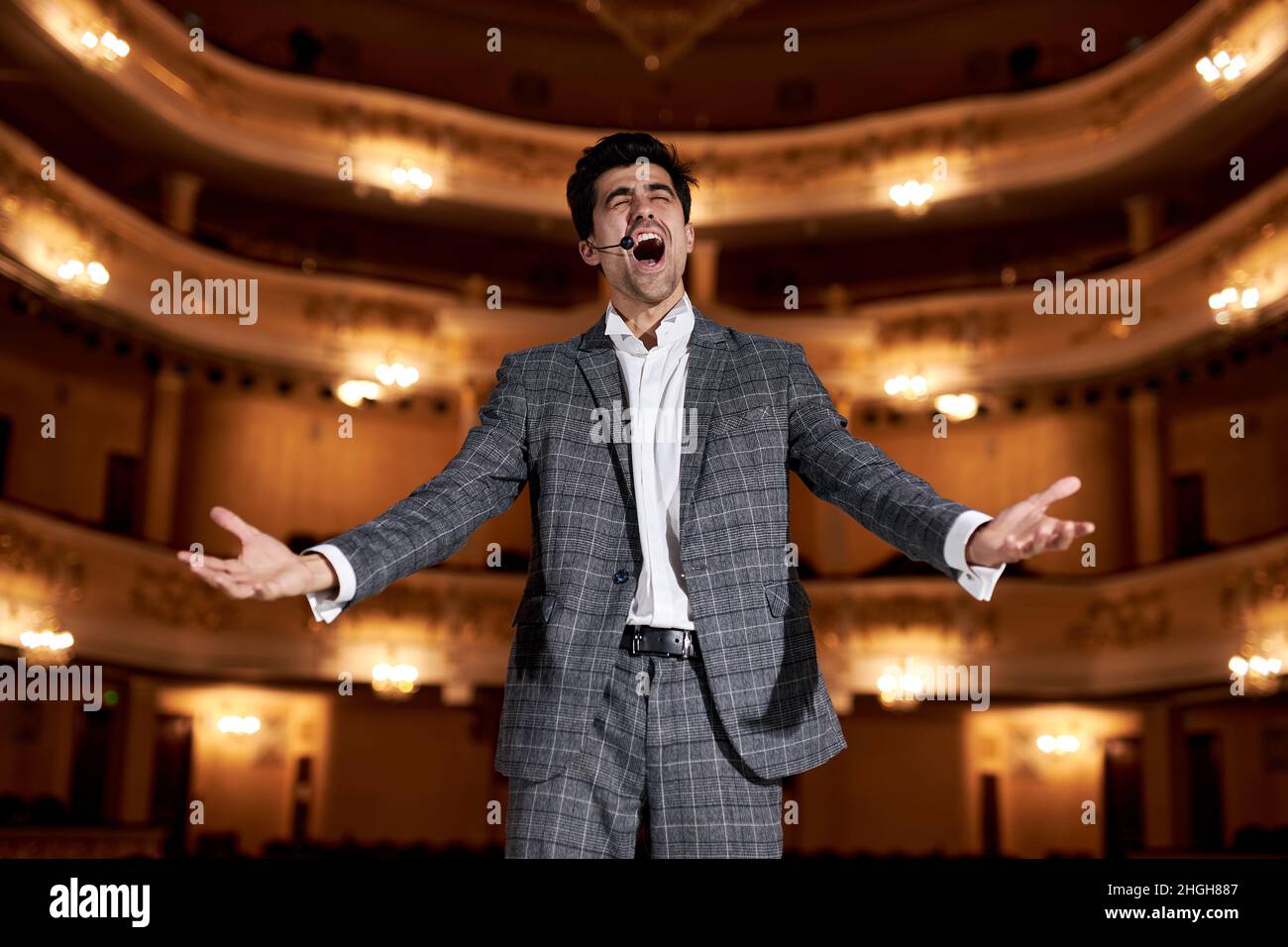 young man in suit gesticulating and singing to audience in theater ...