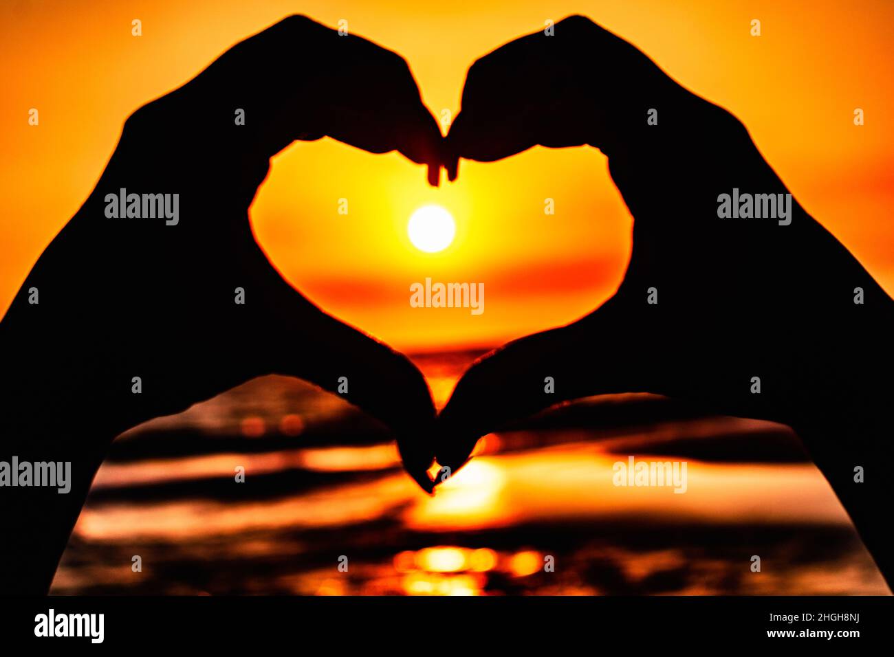 Hand Model making a heart under the sun set with the sun at the middle ...