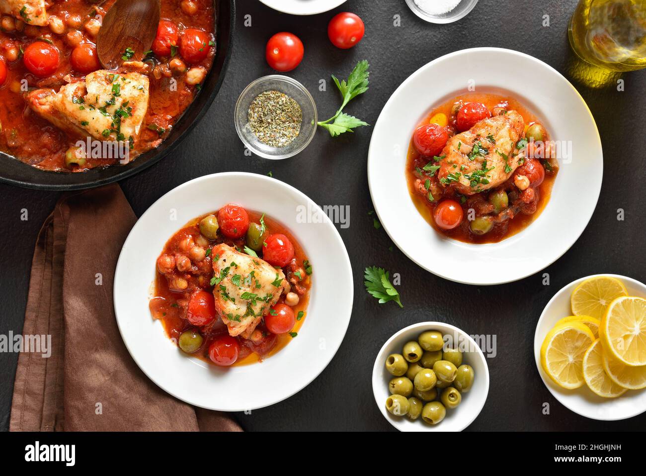 Cod stew with chickpeas, cherry tomatoes and olives over dark stone ...
