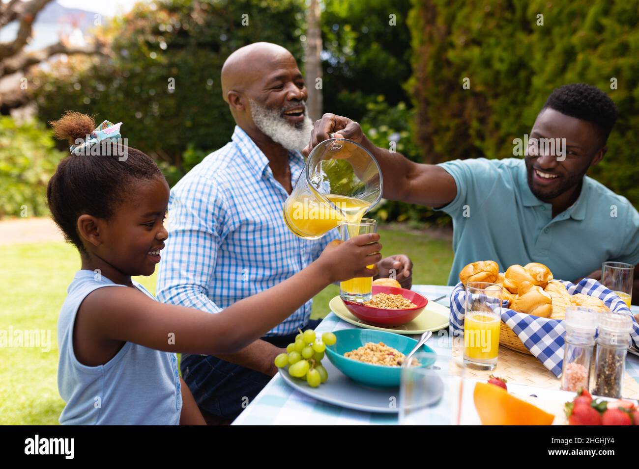Smiling african american man serving juice for daughter by senior man ...
