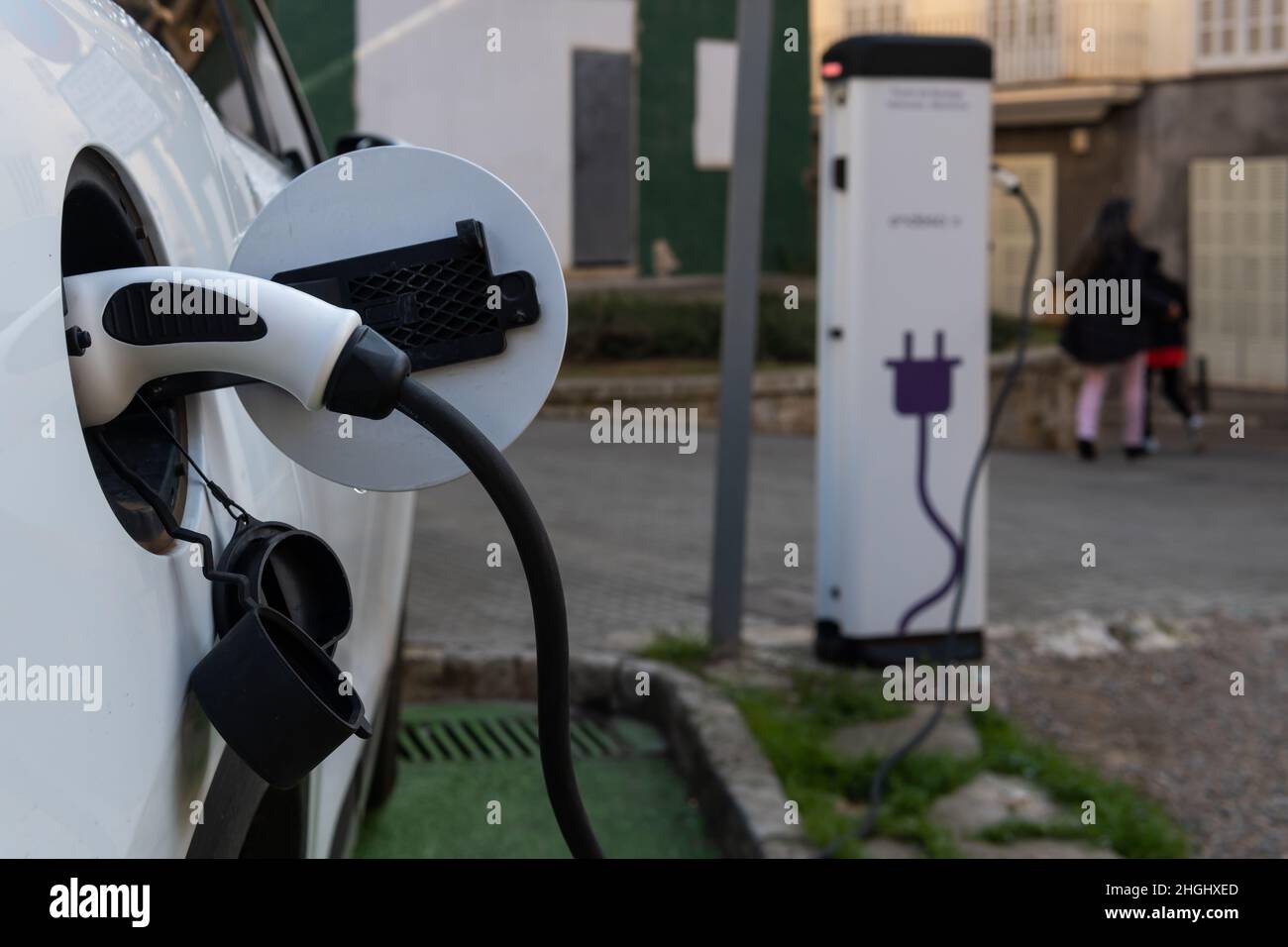 Close-up of a charger charging a white electric car, parked on the ...