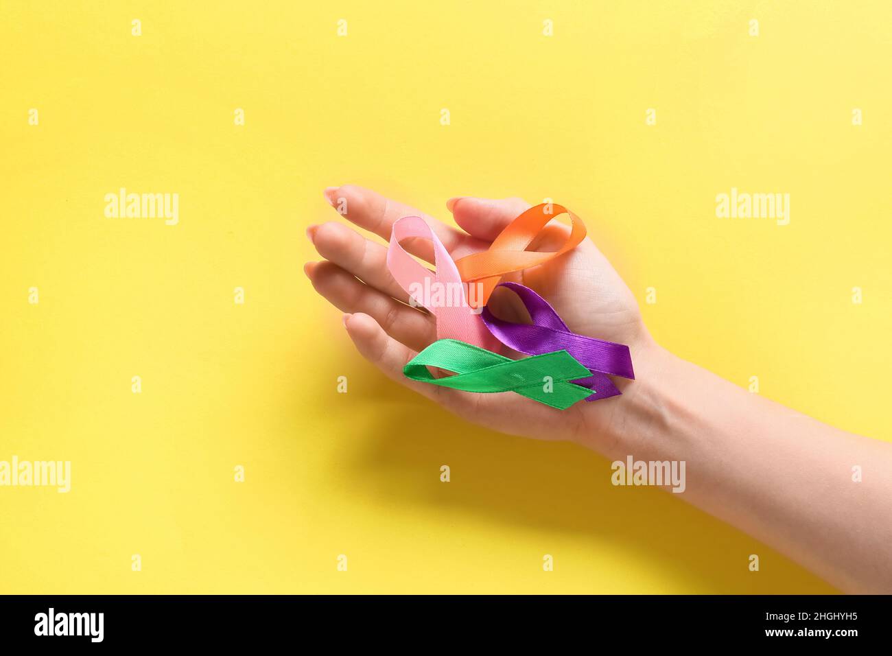 Female hand with different awareness ribbons on yellow background ...