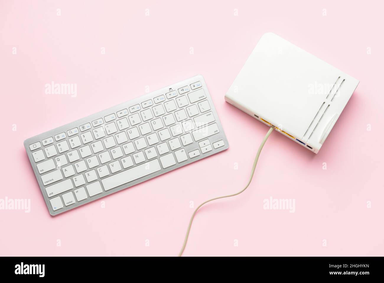 Wi-fi router with internet cable and computer keyboard on pink ...
