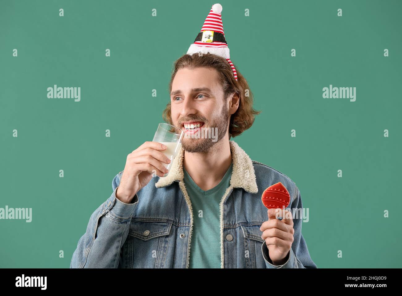 Handsome man with gingerbread cookie drinking milk on green background ...