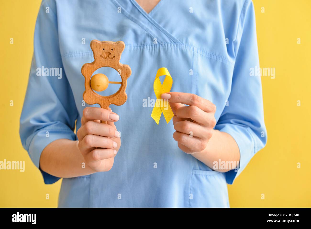 Female nurse holding golden awareness ribbon and rattle on color ...