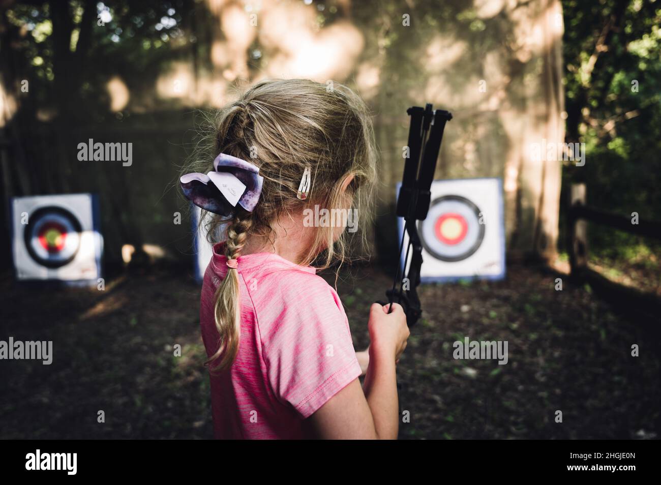 Young girl at summer camp learning to use a bow and arrow looking down ...
