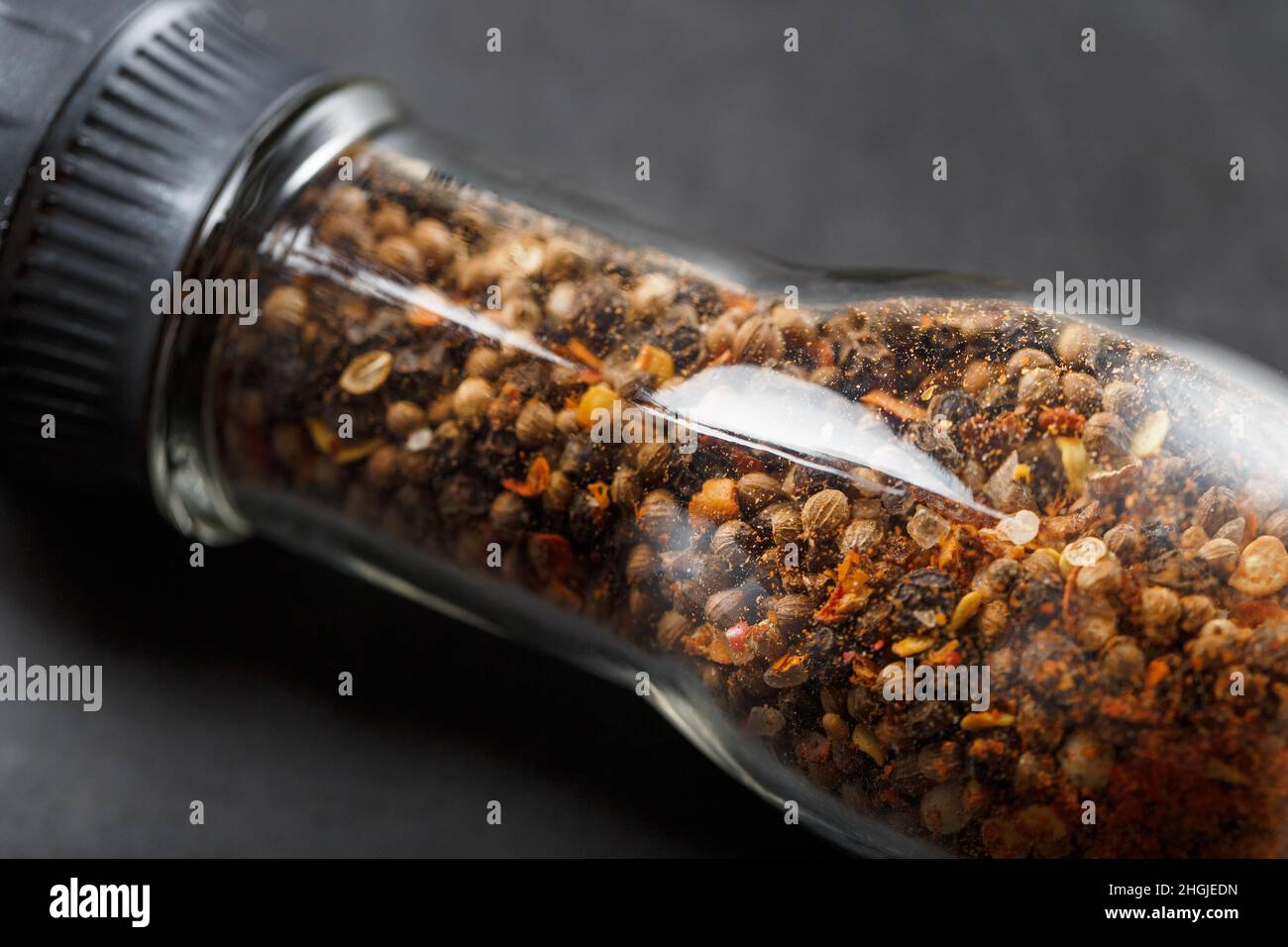 Peppercorns cumin and salt in a transparent mill on a black background ...
