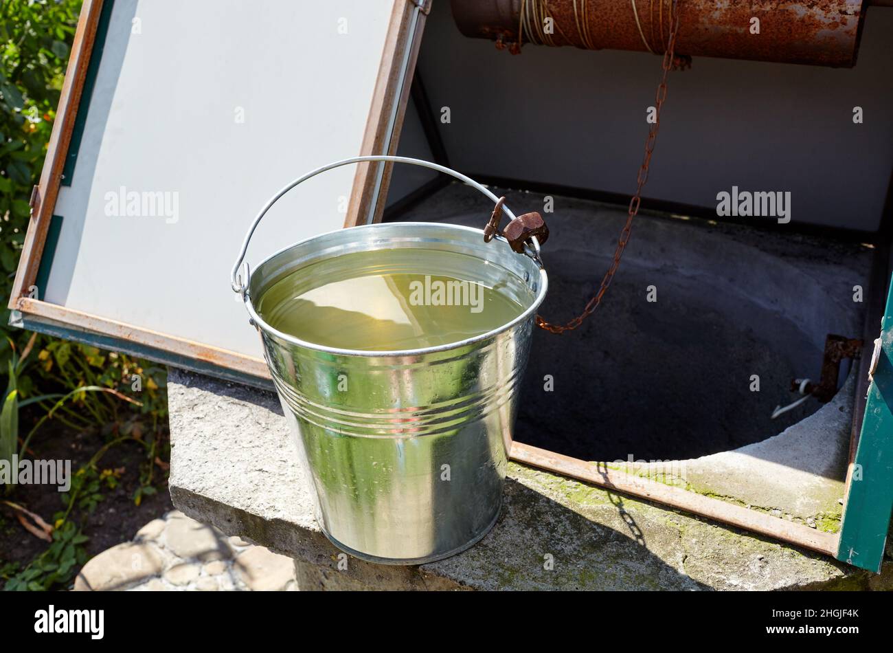 Metal bucket at draw-well in European village. Retro stone water well ...