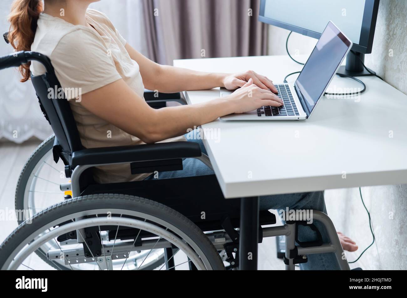 Caucasian woman in a wheelchair typing with a laptop from home. Remote ...