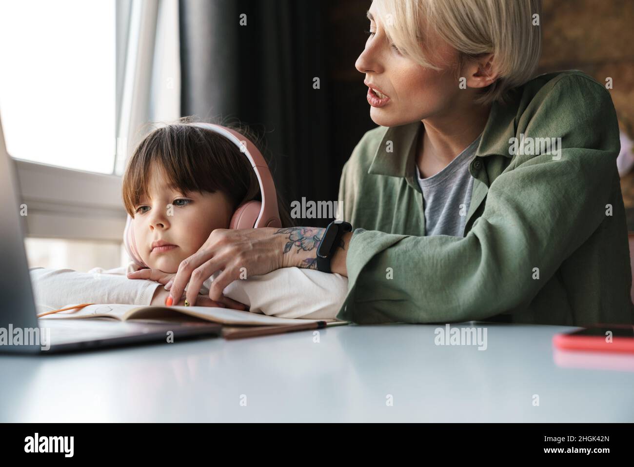 Mother helping her daughter with school homework, using laptop computer ...