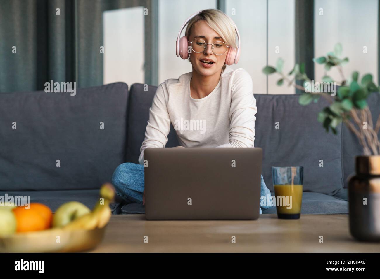 Smiling mid aged blonde woman in headphones studying online via laptop ...