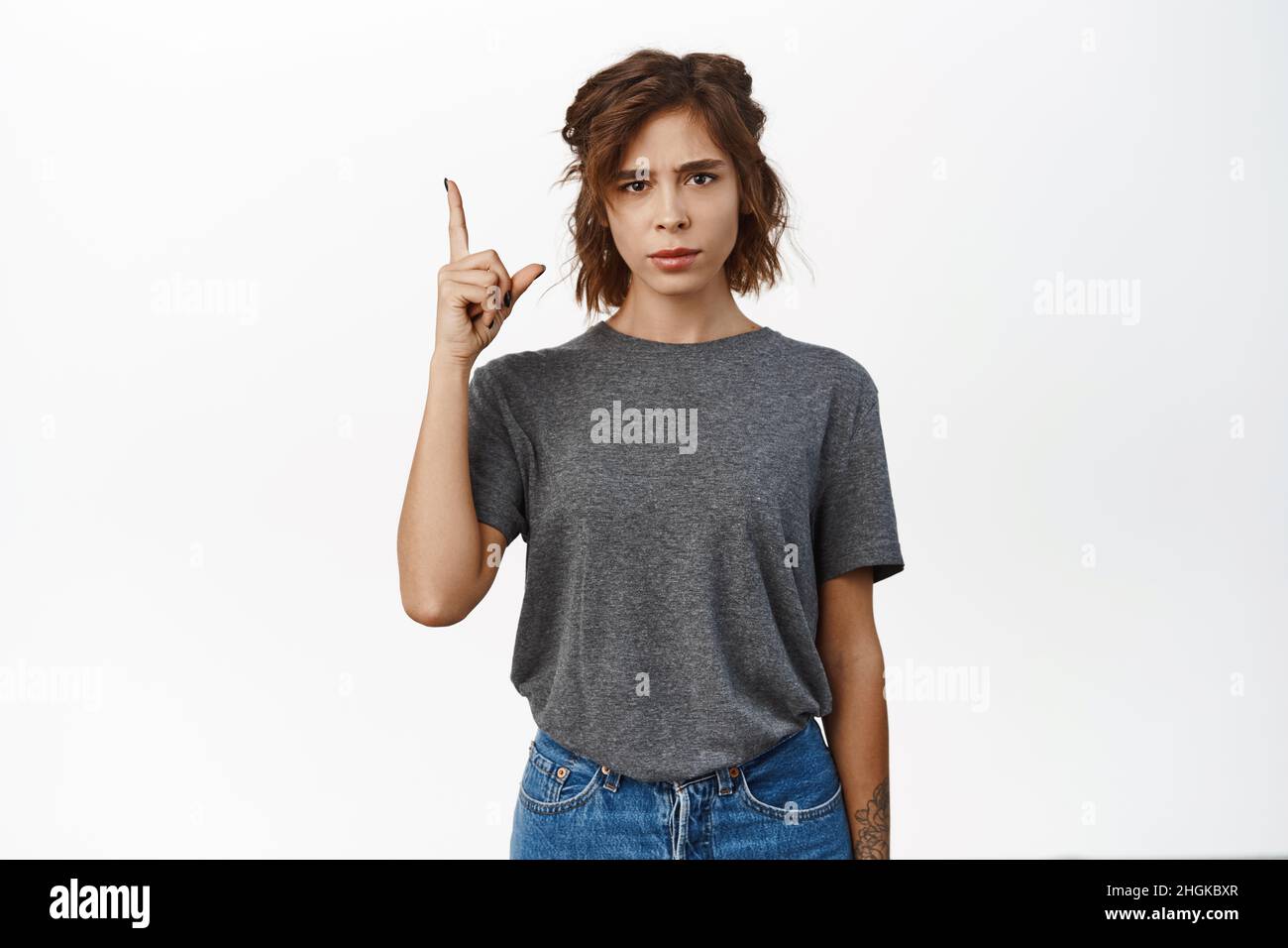 Confused young woman asks question when points finger up, see smth ...