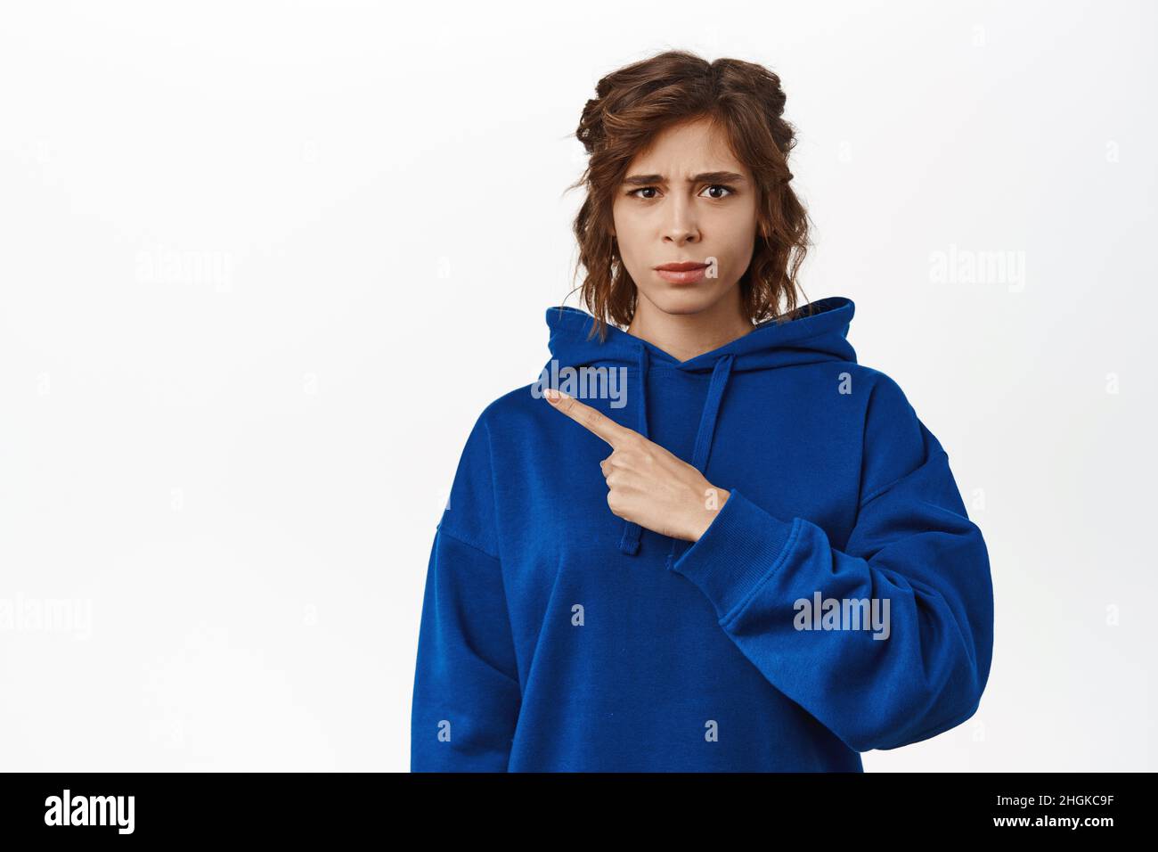 Woman with doubts pointing finger left, looking skeptical, frowning ...