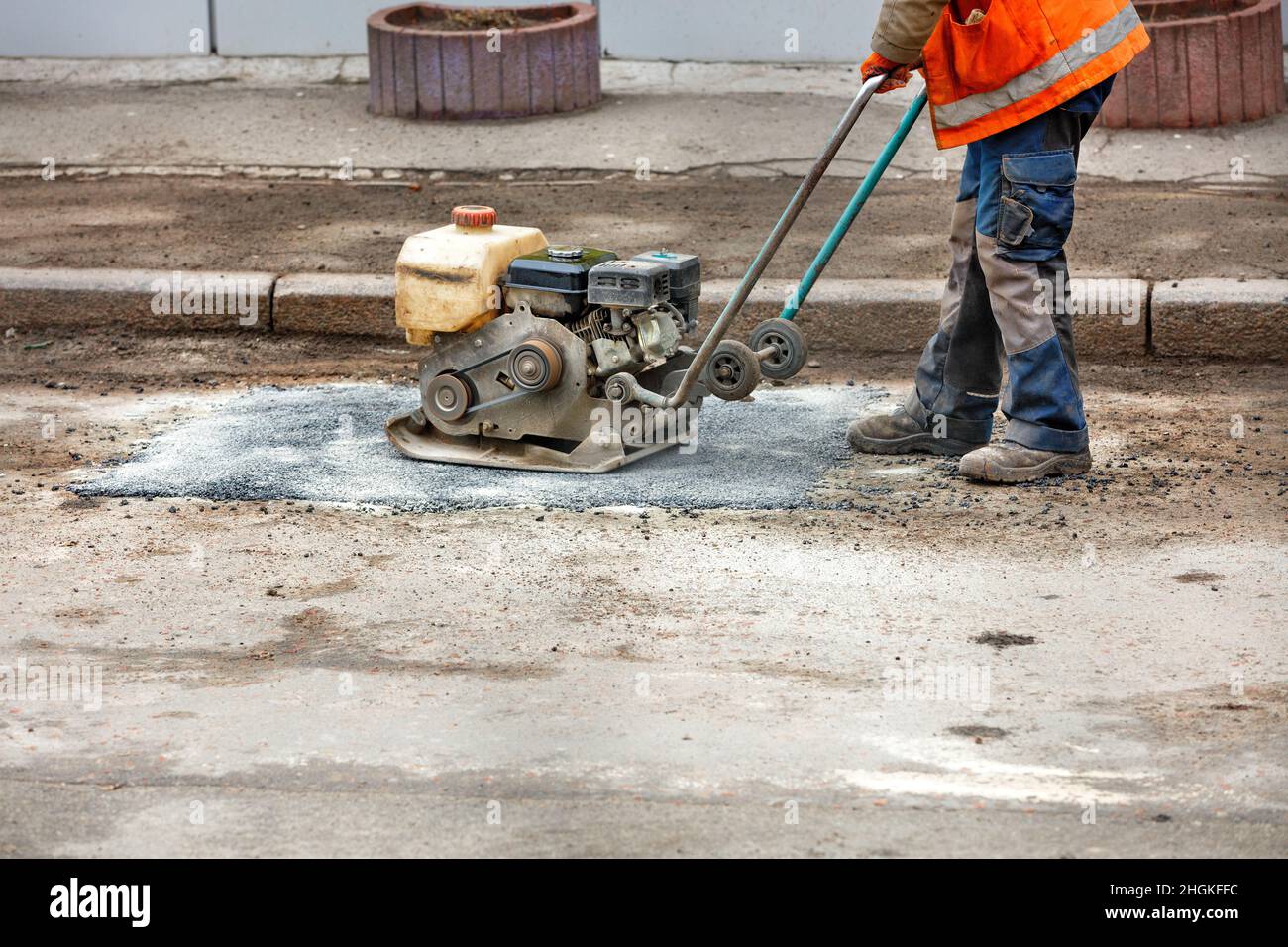 A worker with an old vibrating plate for road construction repairs ...