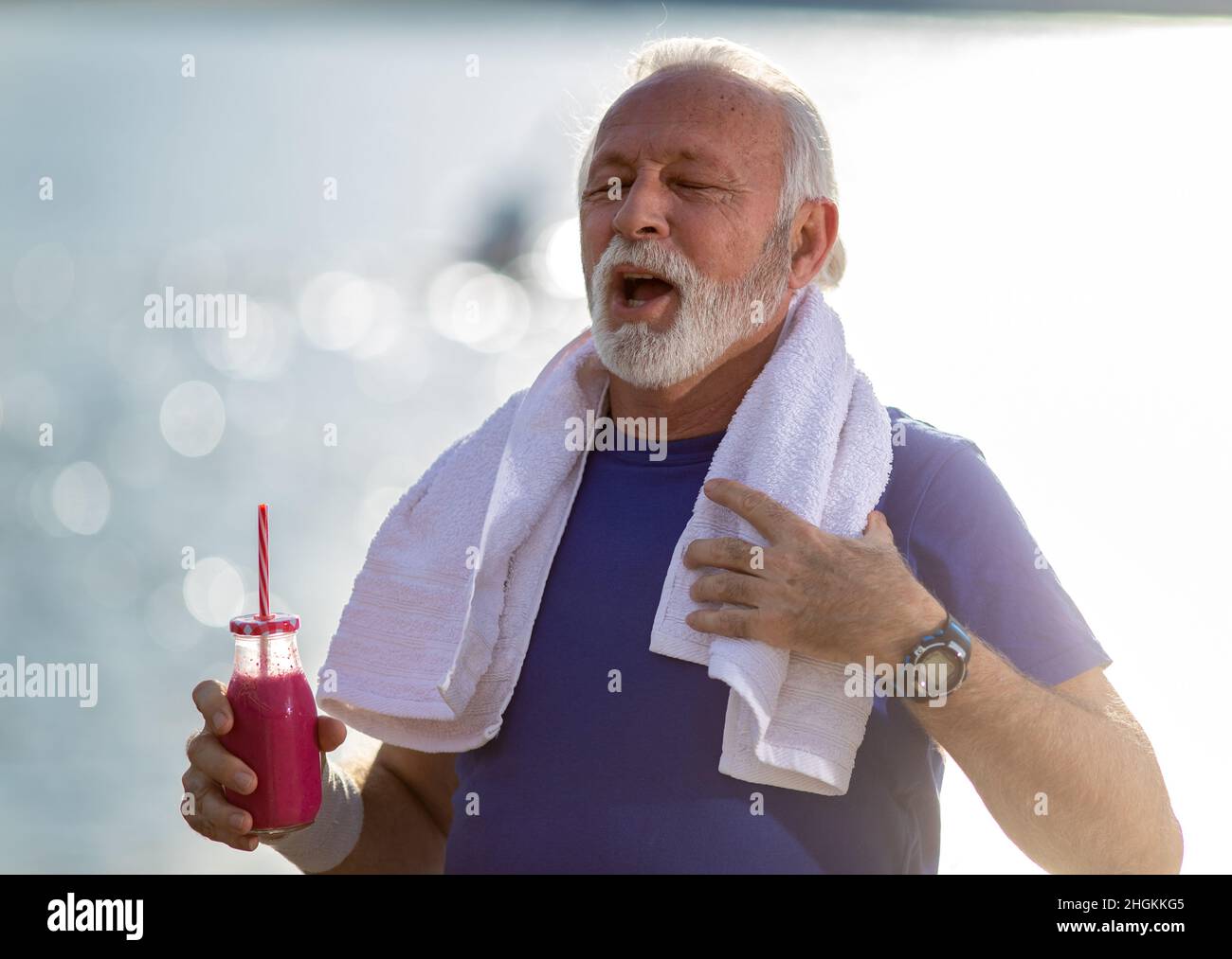 Exhausted senior man with beard drinking fresh juice from bottle with ...