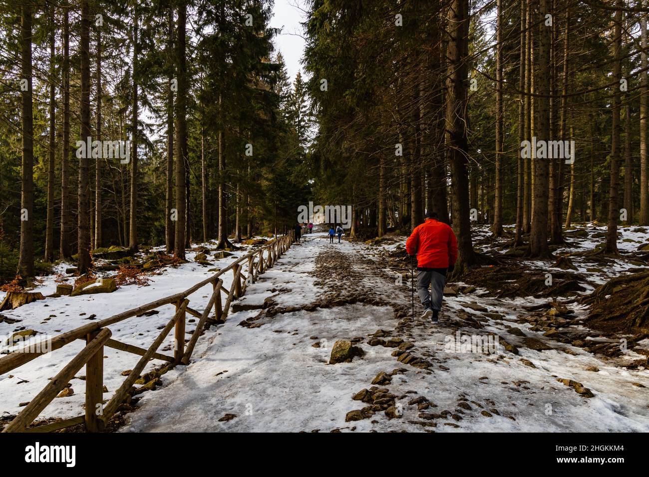People walking through icy mountain trail next to wooden fence and high ...