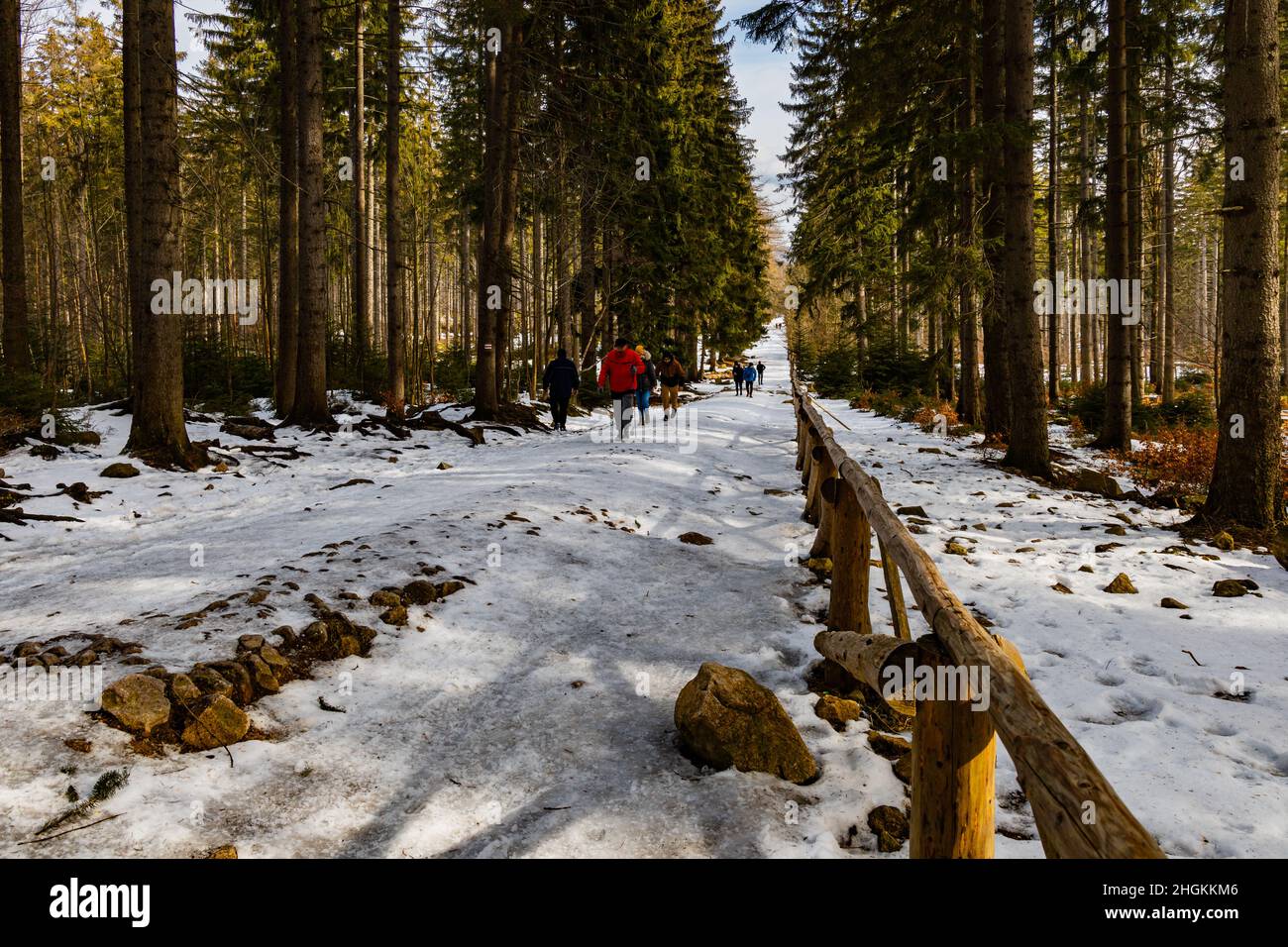 People walking through icy mountain trail next to wooden fence and high ...