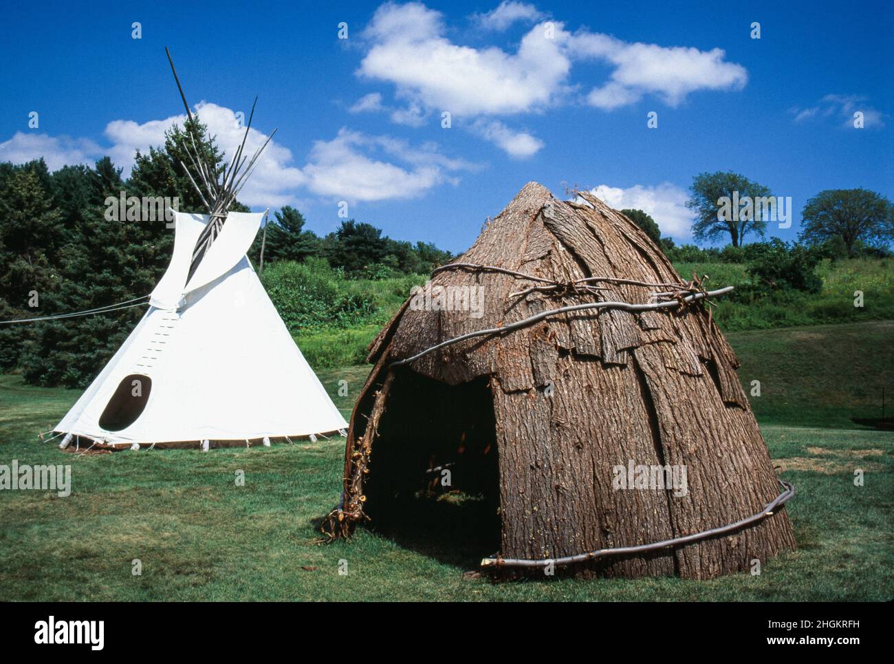 A wigwam and tepee stand in a field at the Fruitlands museum on a sunny ...