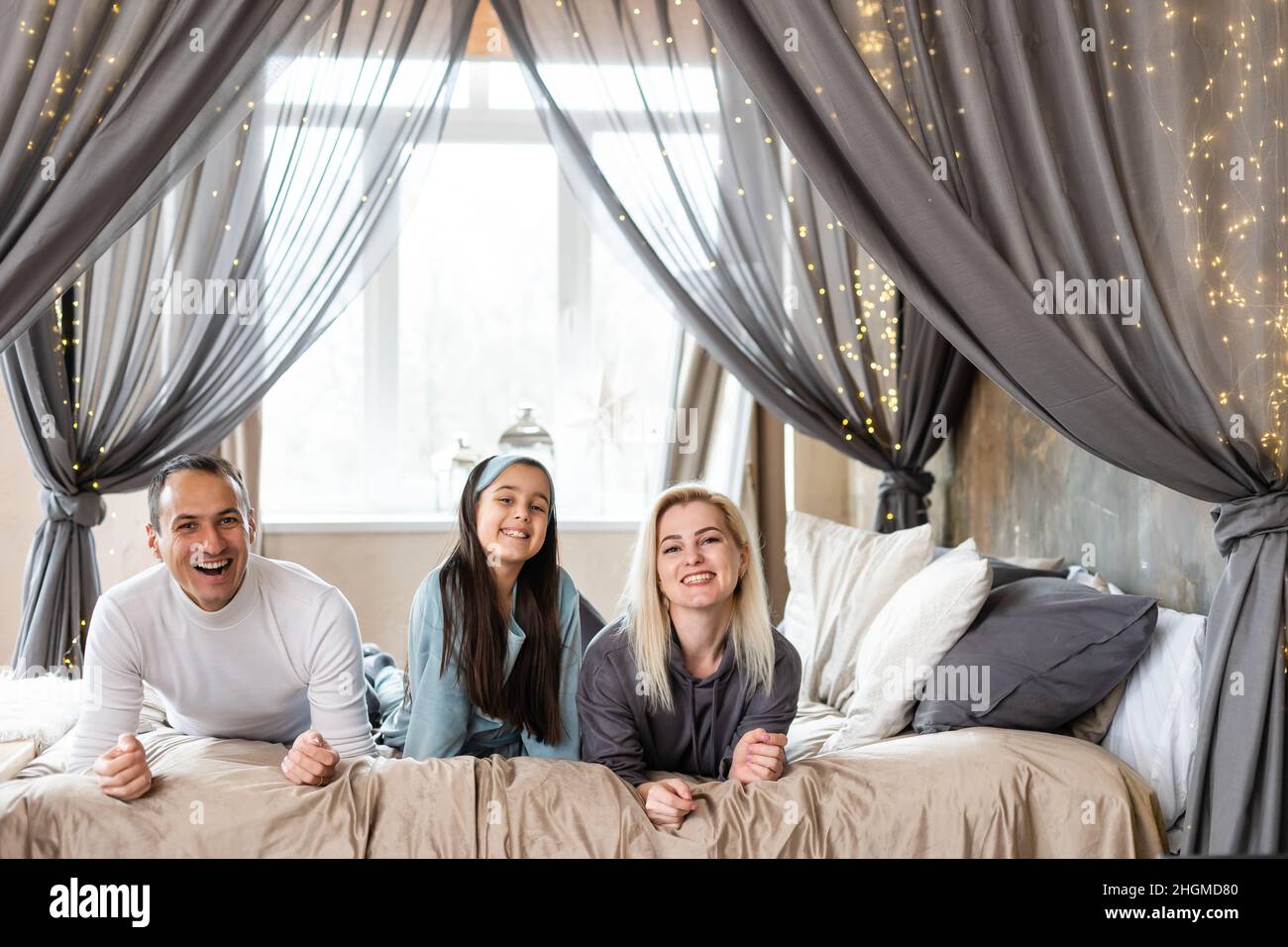 Smiling family lie on a white bed Stock Photo - Alamy