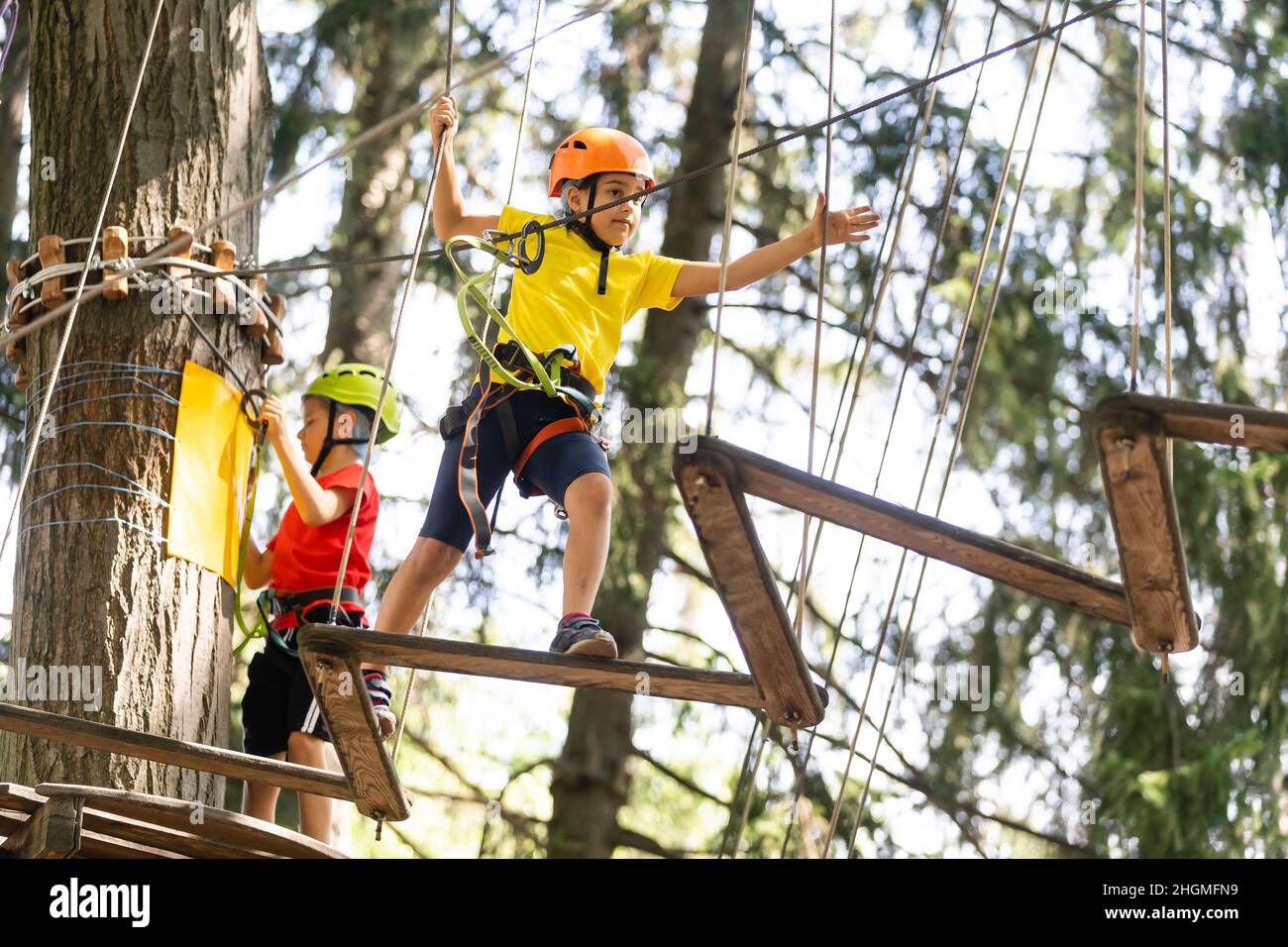 Child in forest adventure park. Kids climb on high rope trail. Agility ...