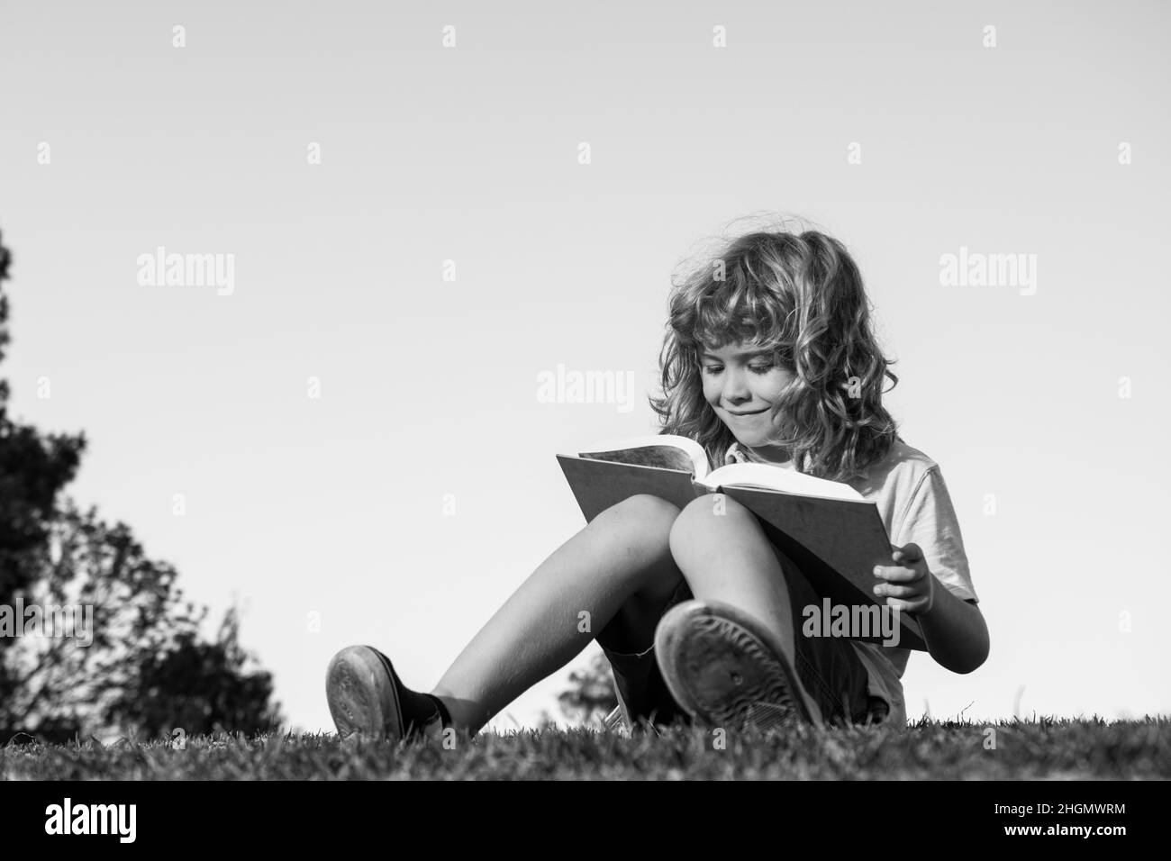 Smart kid boy reading book in park outdoor Stock Photo - Alamy
