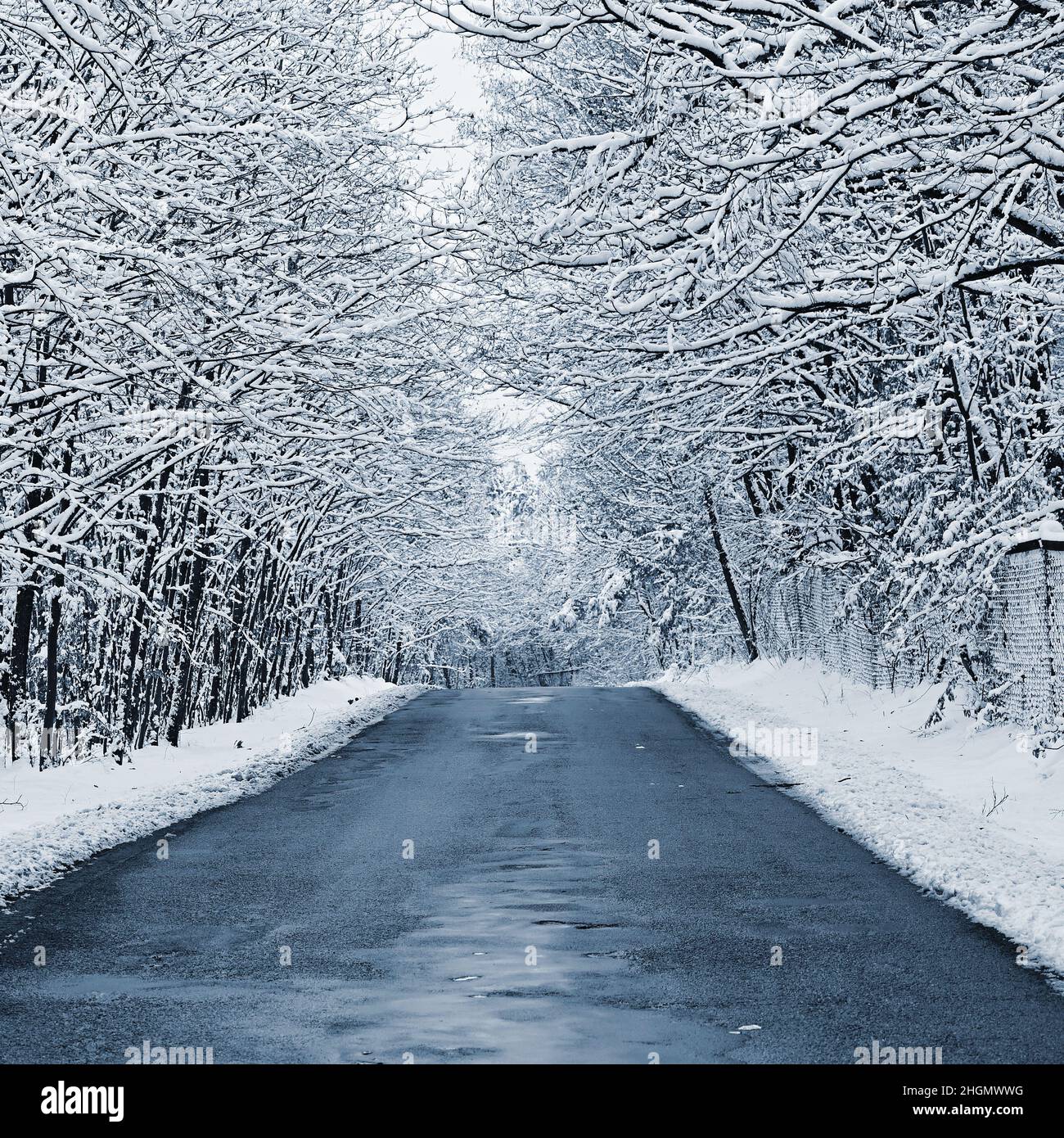 Broken, repaired poor quality asphalt road in winter with snow and ...