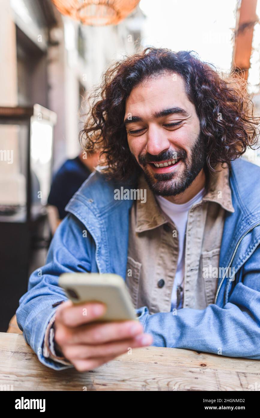 Cheerful Hispanic male in casual outfit with curly hair smiling and ...