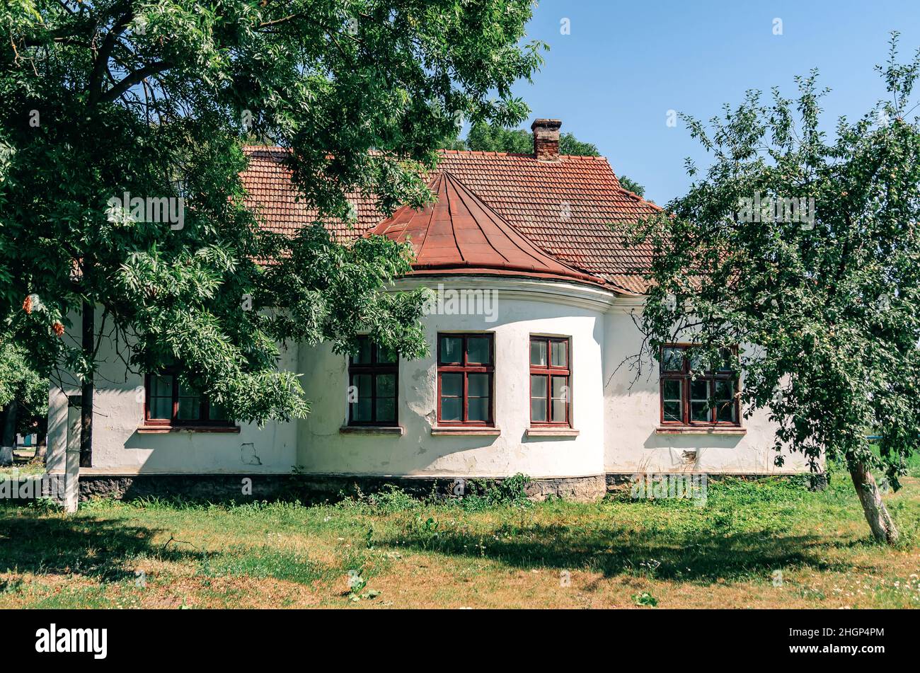 Empty old abandoned building under big green trees. Roof tiles, brick ...