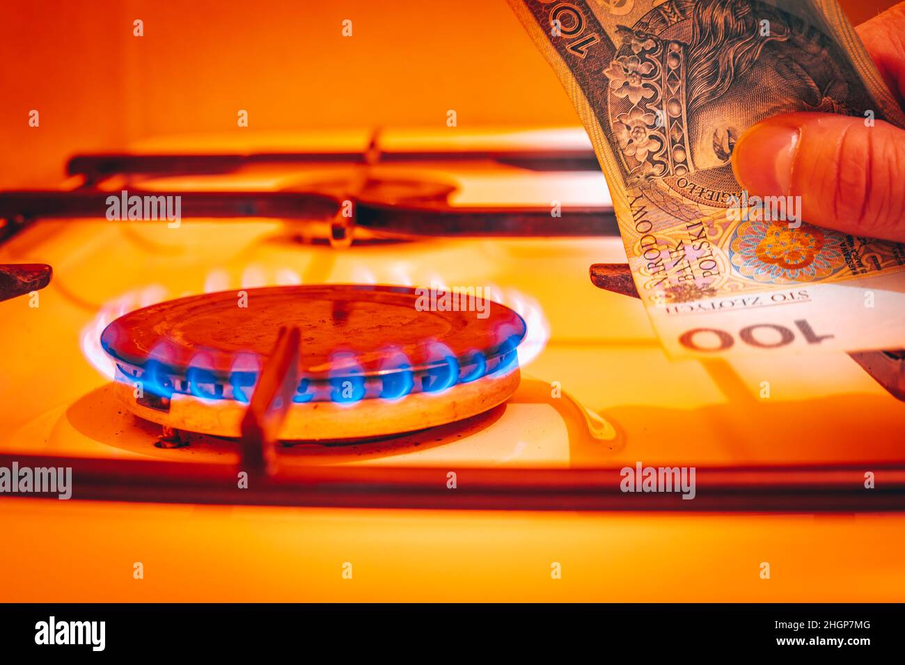 A lit gas stove with a Polish banknote of PLN 100 in hand, Concept of ...