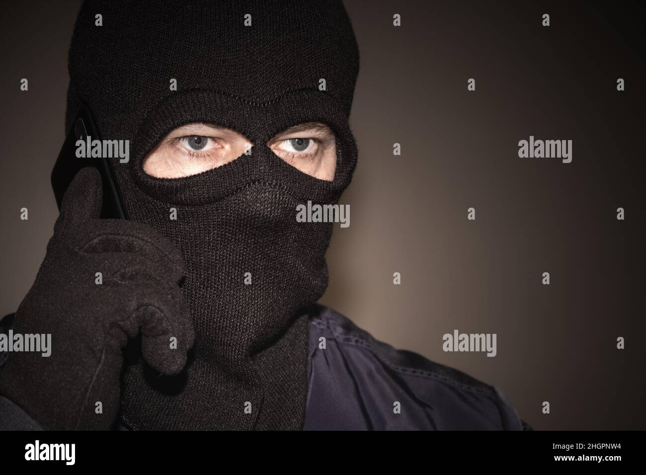 An extortionist in black clothes with a balaclava covering his face. A ...