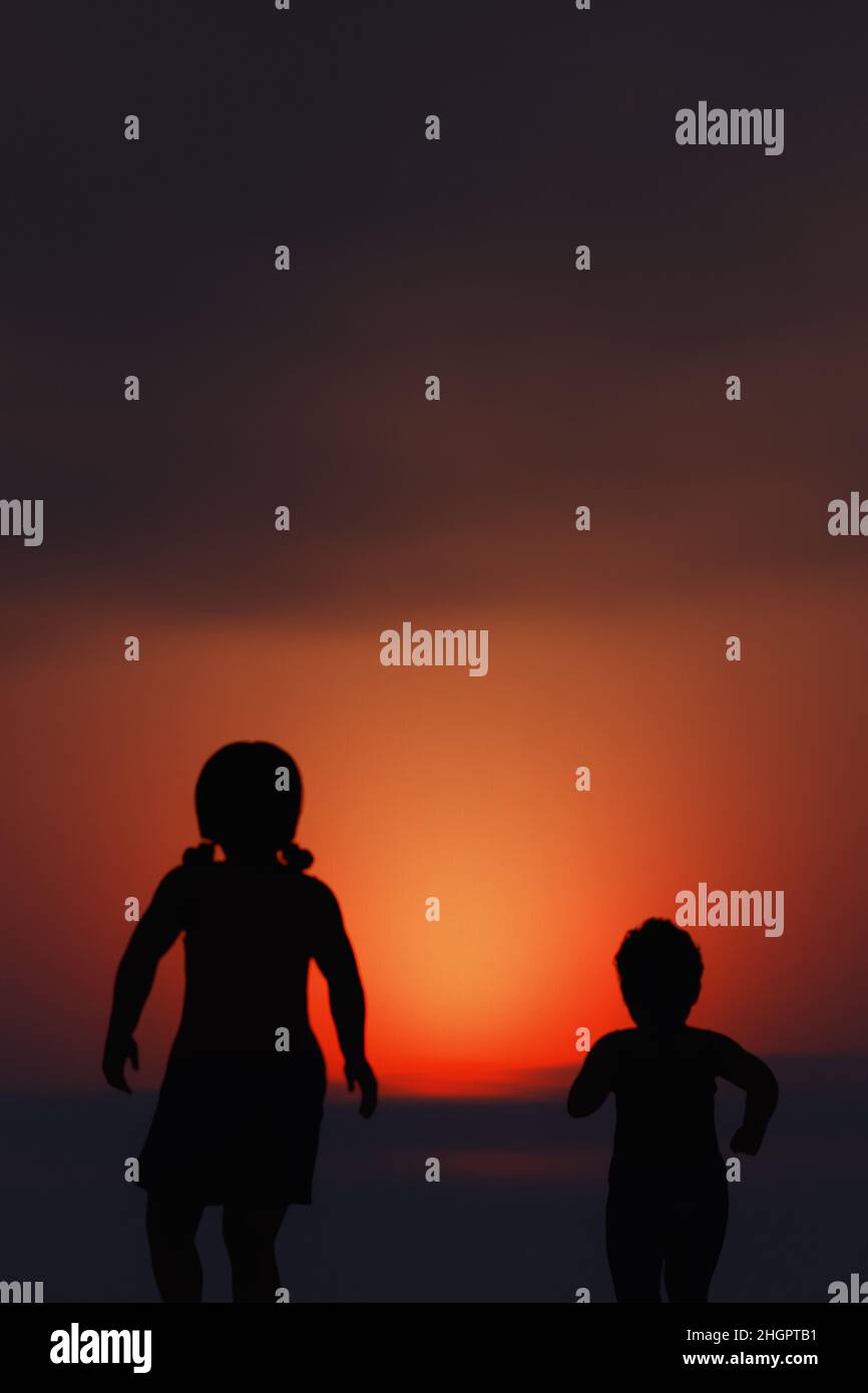 Silhouette of two children running towards the sunset Stock Photo - Alamy