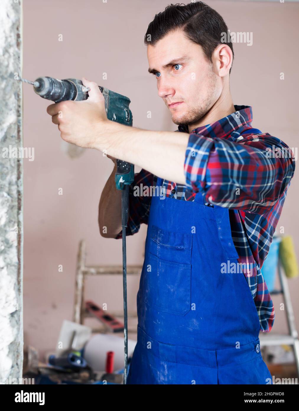 serious professional builder drilling hole in wall with perforator ...