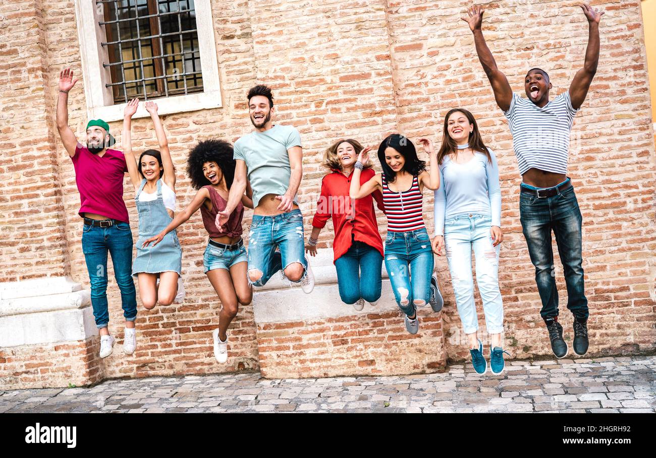 Multicultural milenial friends jumping and cheering against brick wall ...