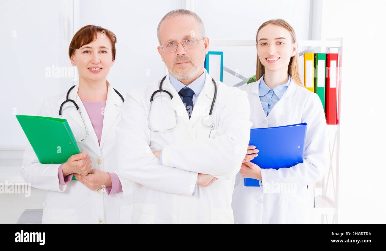 doctor posing in office with medical staff, he is wearing a stethoscope ...